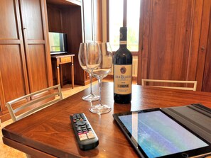 Uma mesa de madeira com um controle remoto, dois copos de vinho, uma garrafa de vinho San Biagio 2018 e um tablet.