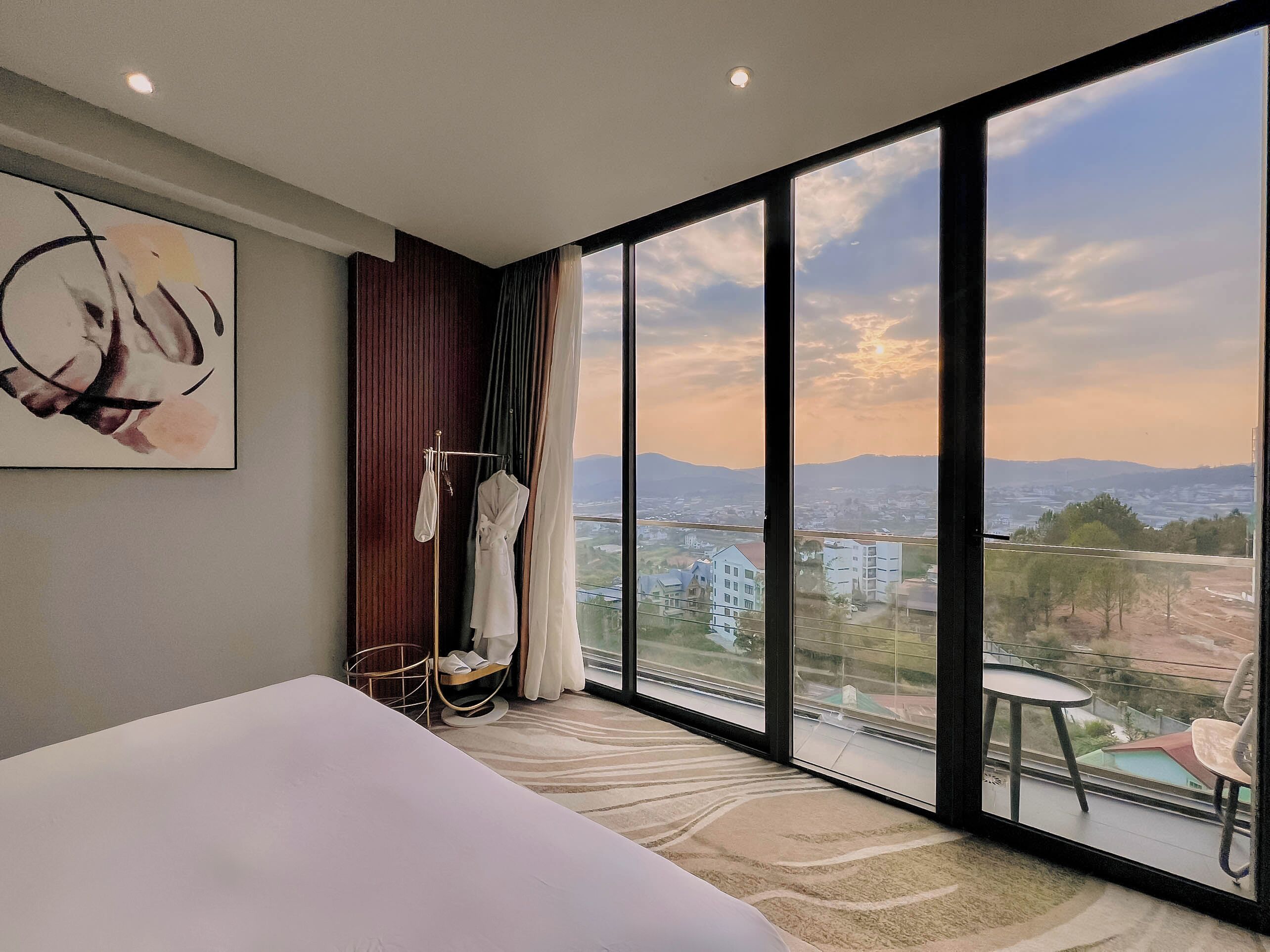 Quarto de hotel com cama grande, vista para a cidade e varanda com uma cadeira.