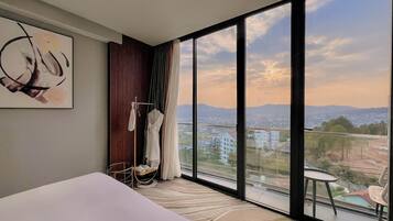 Quarto de hotel com cama grande, vista para a cidade e varanda com uma cadeira.