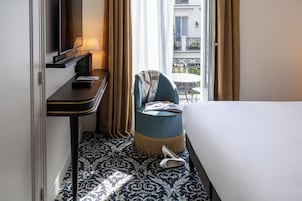 Quarto de hotel com cama, escrivaninha com luminária, cadeira e vista para a varanda externa.