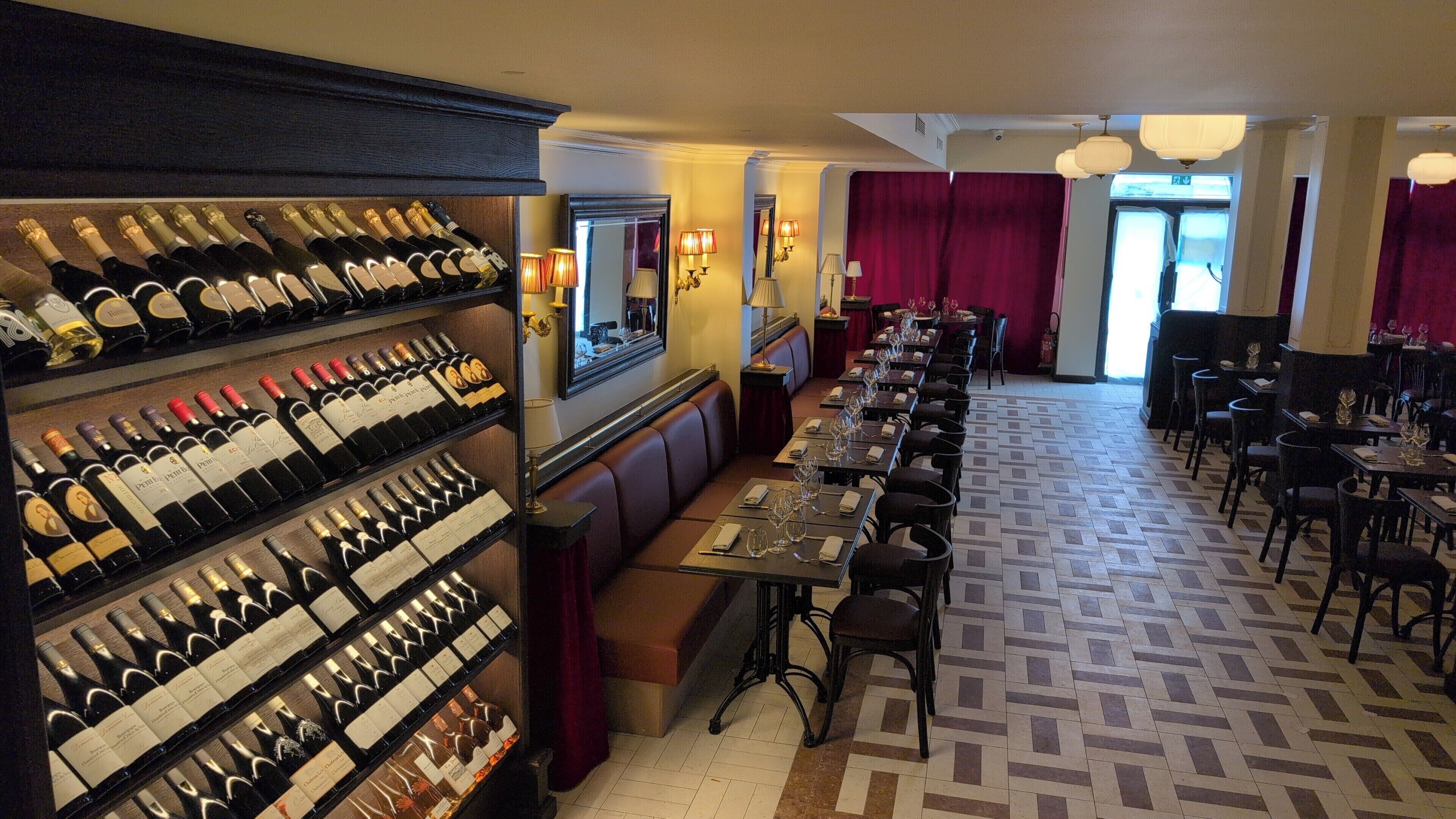 Um restaurante com um balcão comprido, várias mesas e uma seleção de vinhos.