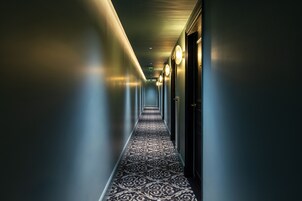 Um corredor comprido e estreito, com carpete estampado e portas em um dos lados.