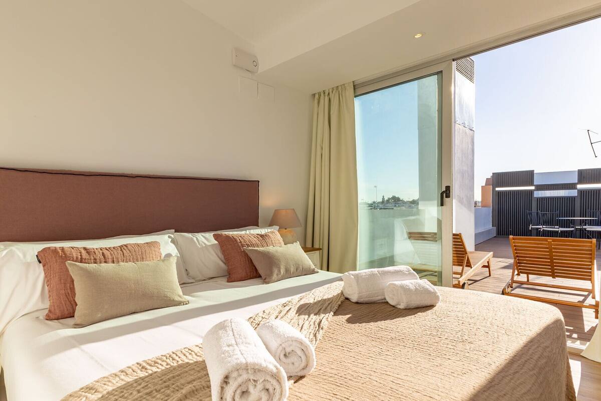 Quarto de hotel com uma cama grande, duas mesas de cabeceira, uma porta de vidro que dá para uma área de estar ao ar livre e vista para a cidade.