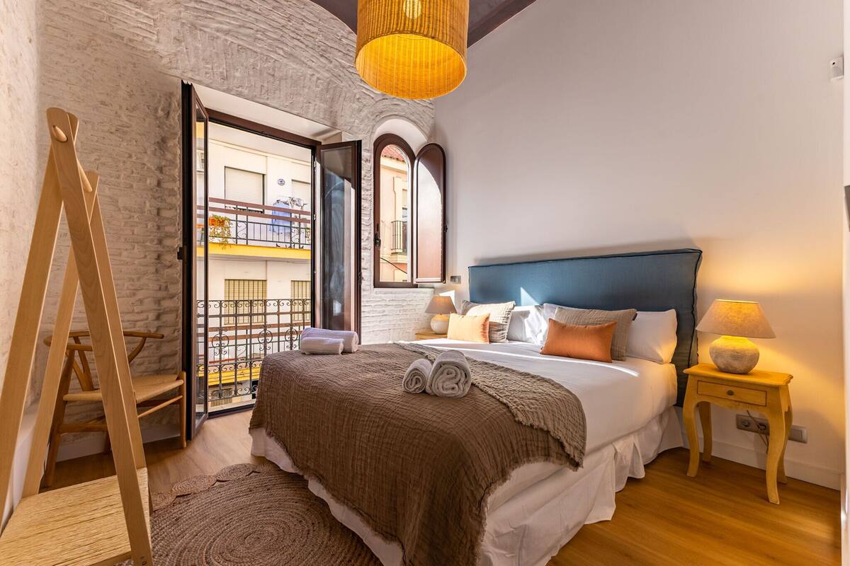 Quarto com uma cama grande, uma escada de madeira, um candeeiro pendente e vista para a varanda.