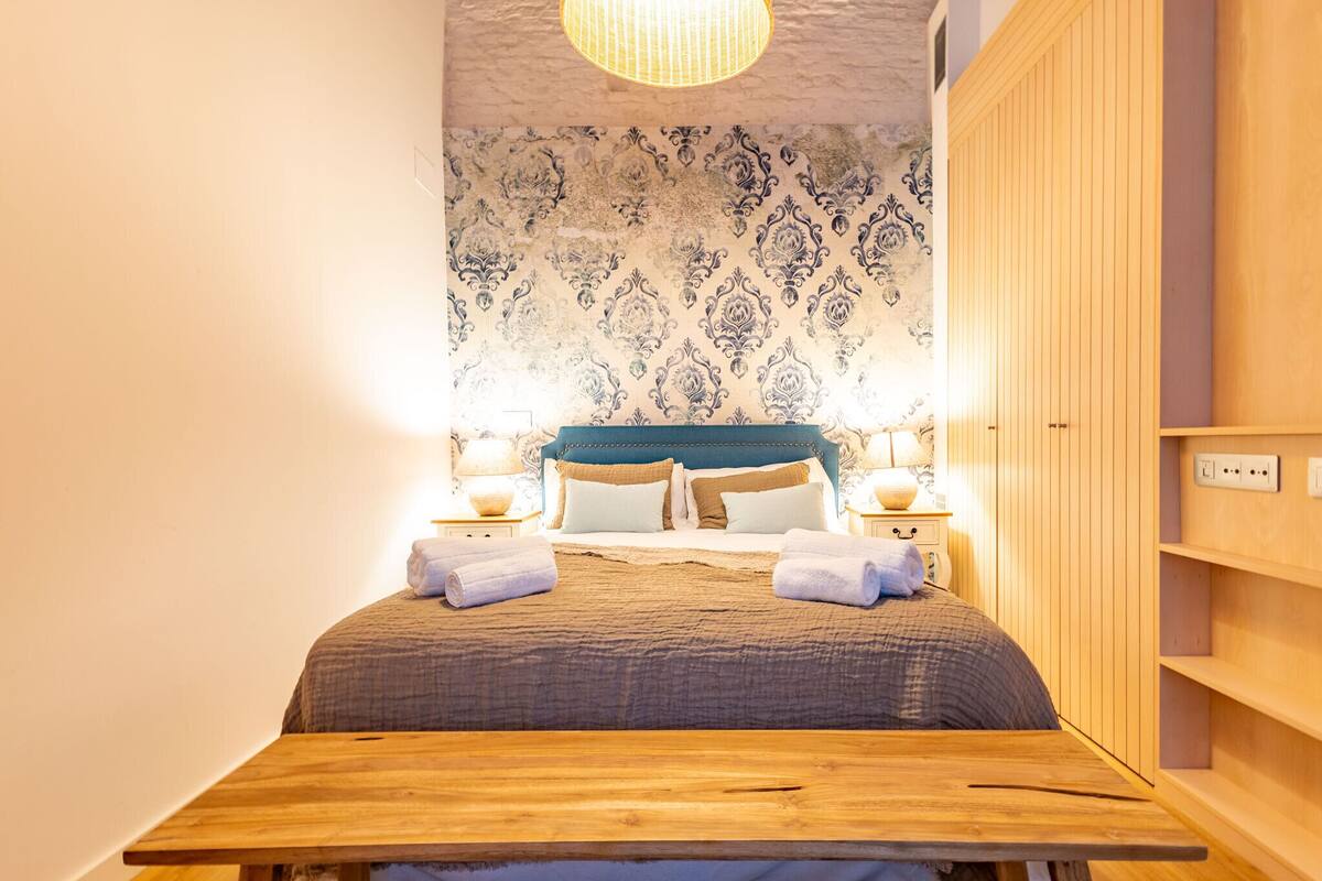 Cama bem arrumada com cabeceira estampada, abajures e mesa de cabeceira de madeira.