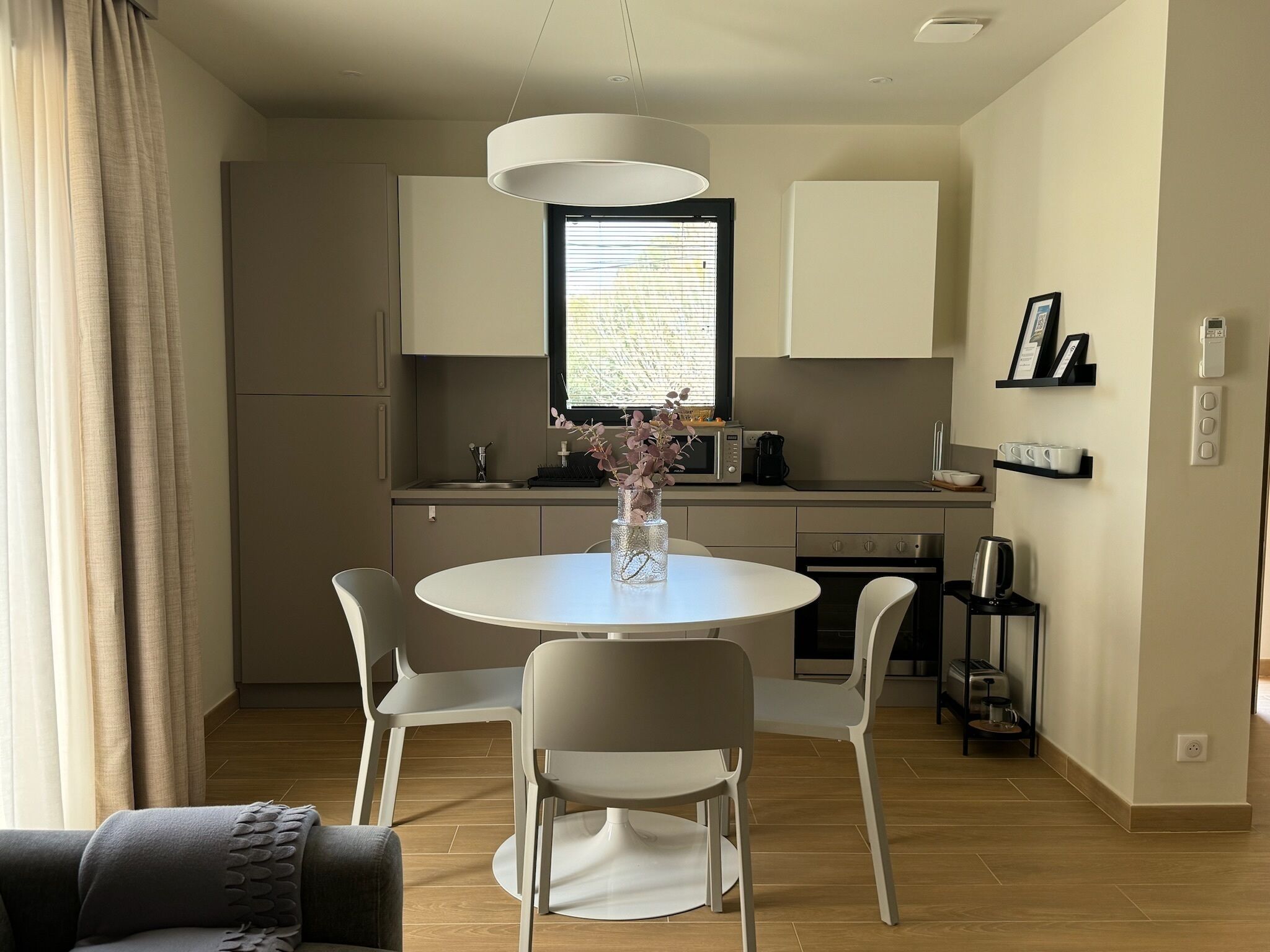 Cozinha moderna com área de jantar, com uma mesa redonda, cadeiras brancas e uma luminária pendente.