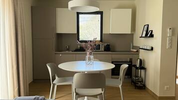 Cozinha moderna com área de jantar, com uma mesa redonda, cadeiras brancas e uma luminária pendente.