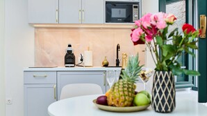 Uma cozinha moderna com micro-ondas, pia e área de refeições com mesa posta, frutas e um vaso de flores.
