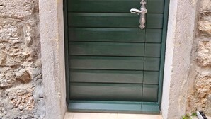 Uma porta verde com puxador de metal, embutida numa parede de pedra, com o número '21' visível acima.
