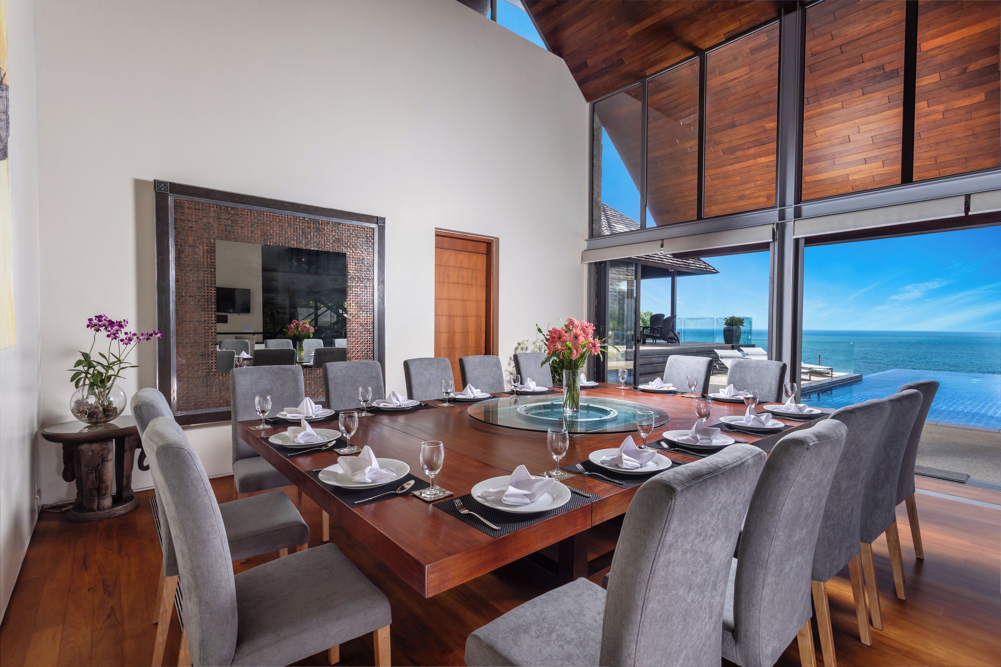Uma sala de jantar moderna com uma mesa grande posta para refeição, grandes janelas e vista para o oceano.