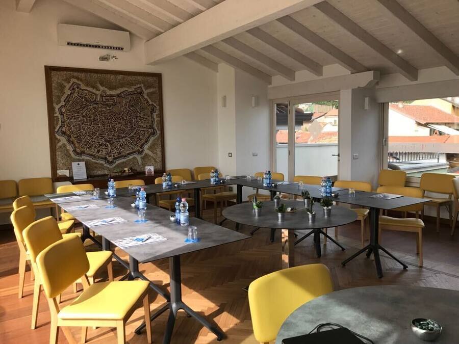 Sala de conferência com várias mesas e cadeiras amarelas, equipada com garrafas de água e papéis.