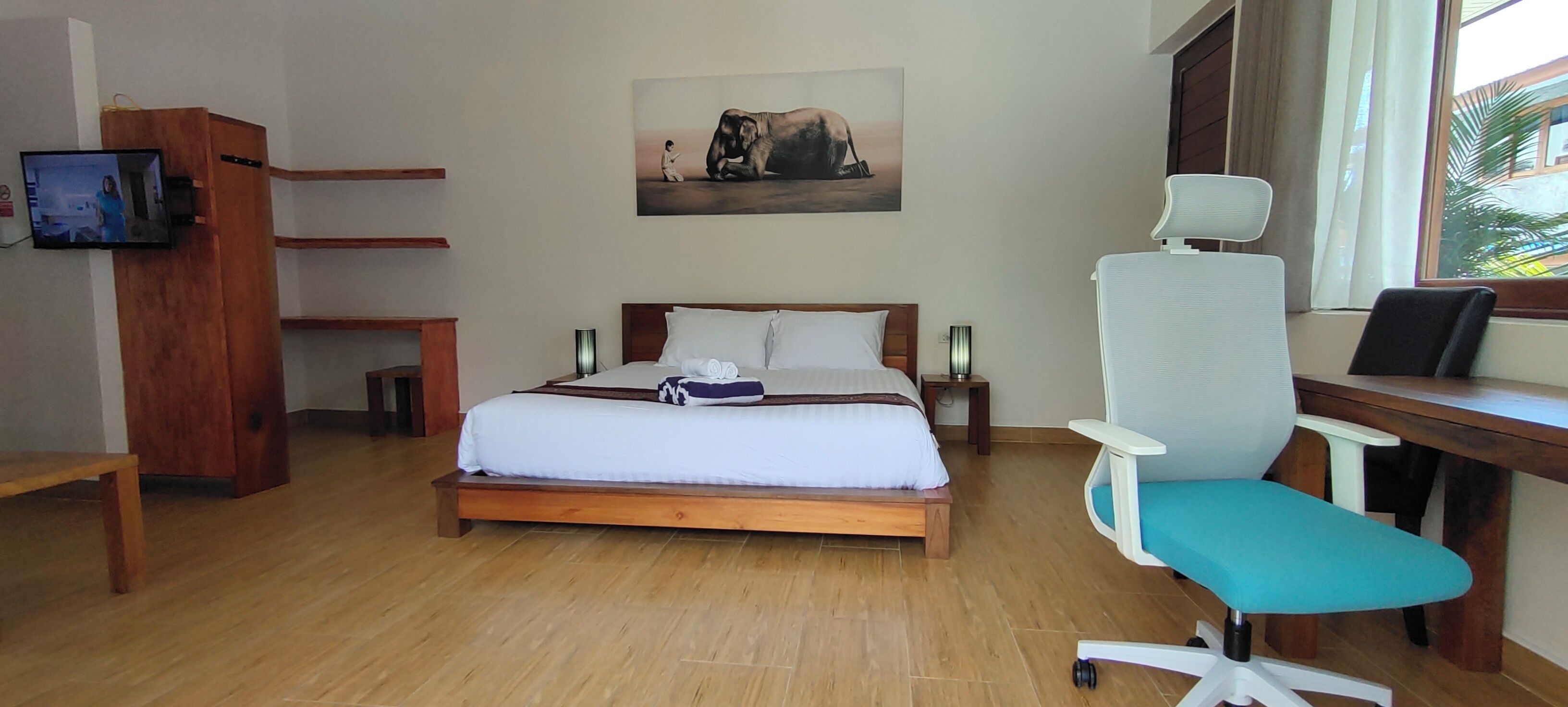 Quarto de hotel com cama, escrivaninha, cadeira, televisão e obras de arte na parede.