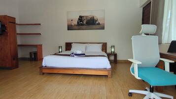 Quarto de hotel com cama, escrivaninha, cadeira, televisão e obras de arte na parede.