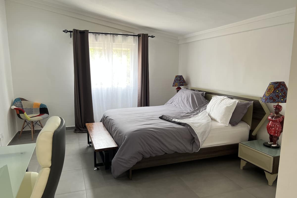 Quarto moderno com cama, mesas de cabeceira, uma cadeira e uma escrivaninha.