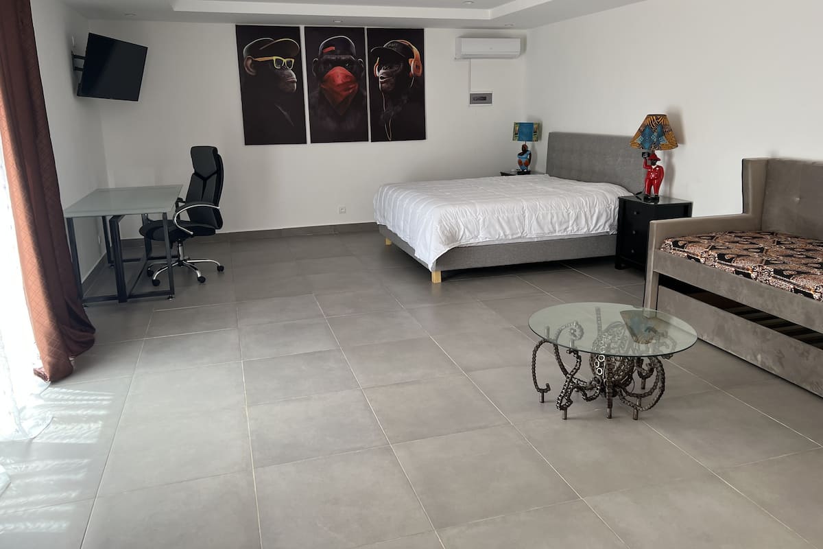 Quarto moderno com cama, escrivaninha, cadeira, mesa de centro de vidro e televisão na parede.
