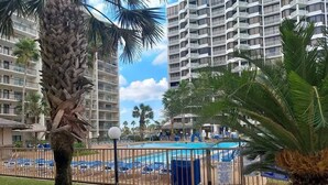 Um hotel com piscina rodeada por palmeiras e uma área cercada com espreguiçadeiras.