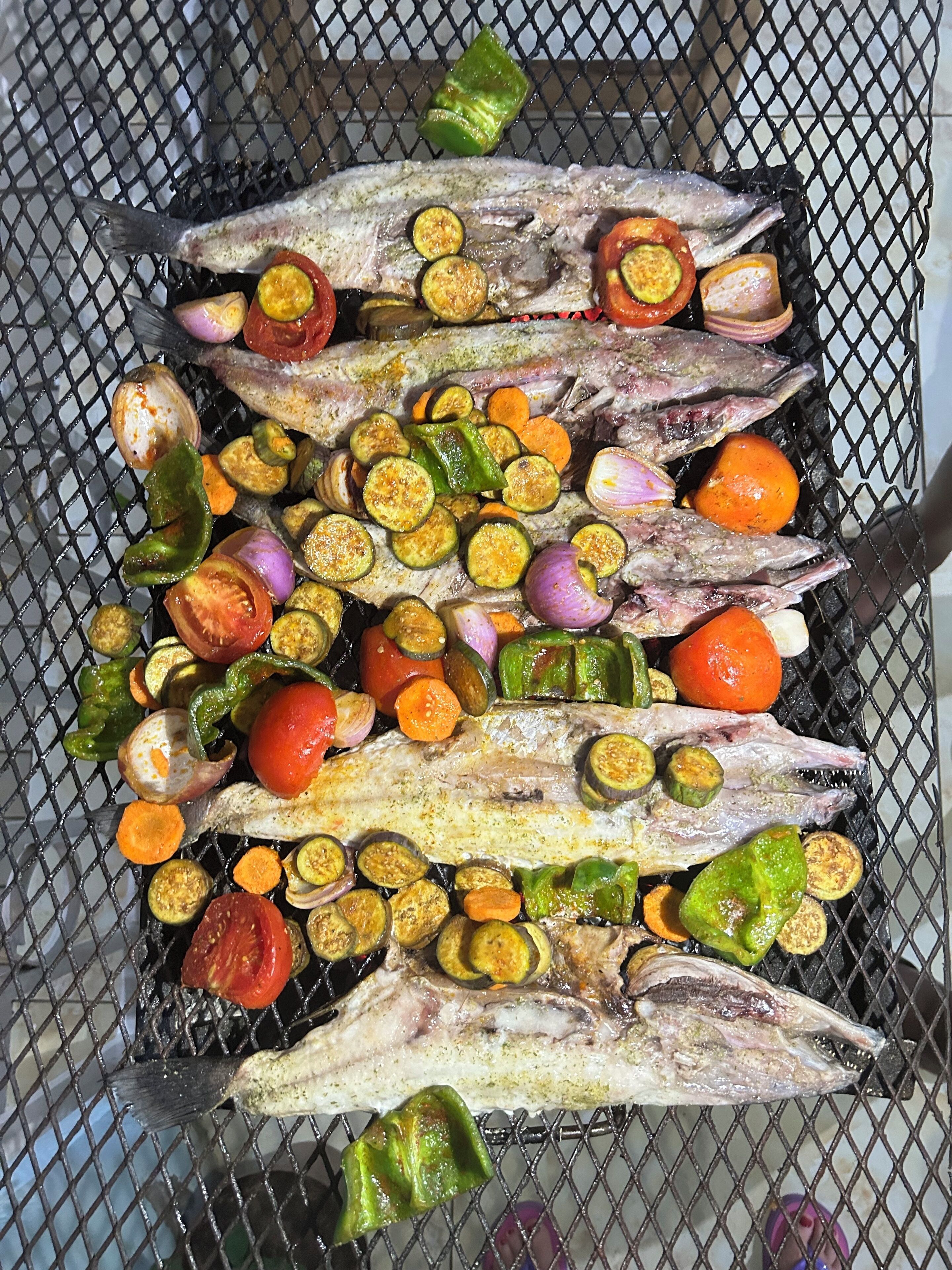 Uma churrasqueira com vários peixes e legumes variados.