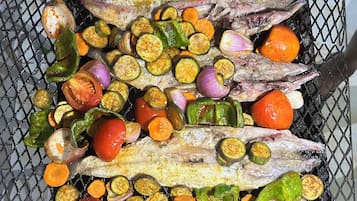 Uma churrasqueira com vários peixes e legumes variados.