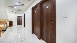 Um corredor moderno com portas de madeira, piso de azulejos brancos e iluminação embutida no teto.