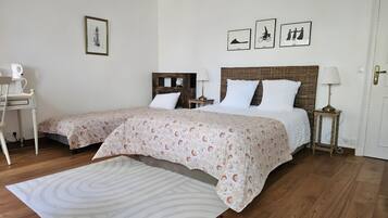 Quarto com duas camas, piso de madeira, tapete branco e parede com quadros emoldurados.
