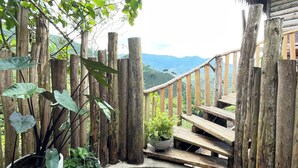 Um deck de madeira com caminho de pedra, plantas em vasos e uma estrutura com telhado de palha.