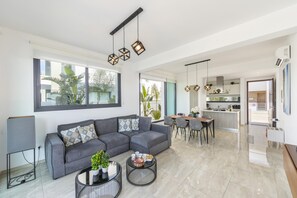 Uma sala de estar moderna com um sofá cinzento, duas mesas de centro e uma área de jantar com uma mesa e cadeiras de madeira.