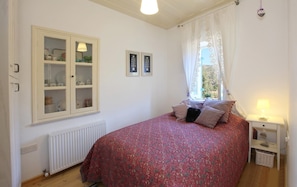 Uma cabana de 3 quartos com uma cama, uma janela com cortinas, um radiador e um armário com portas de vidro.