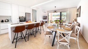 Uma cozinha moderna com armários brancos, uma ilha central com banquetas e uma área de refeições com cadeiras brancas e uma mesa redonda.