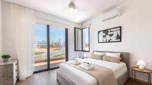 Quarto de hotel moderno com uma cama grande, mesa de cabeceira, luminária e vista para o exterior.