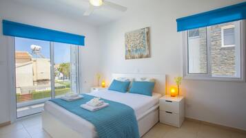 Quarto moderno com uma cama grande, duas mesas de cabeceira, um ventilador de teto e vista para o exterior.