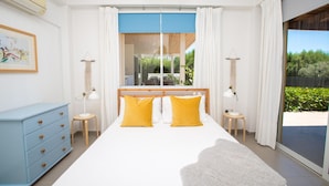 Quarto com cama grande, duas luminárias de cabeceira, cômoda e vista para o exterior.