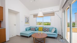 Uma sala de estar moderna com um sofá azul claro, uma mesa de centro de madeira e uma grande janela com vista para o verde.