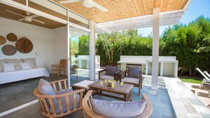 Uma área de estar moderna ao ar livre, com móveis de madeira, parede de vidro e ventilador de teto.