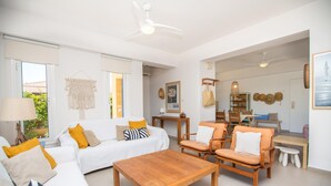 Ampla sala de estar com sofá branco, mesa de centro de madeira e cadeiras laranja.
