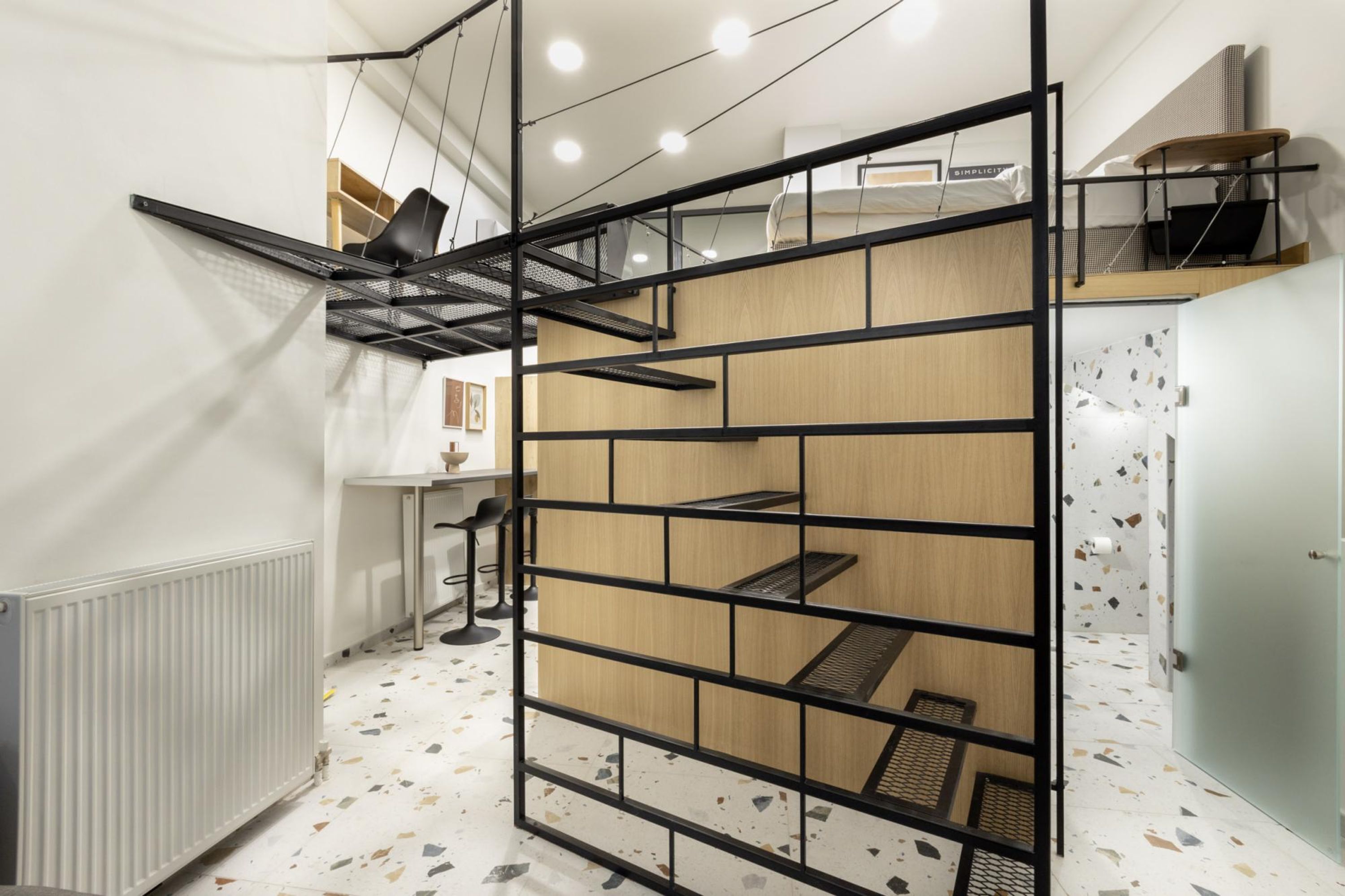 Um interior moderno com um mezanino, um radiador branco e uma área de cozinha com bancada e cadeiras.