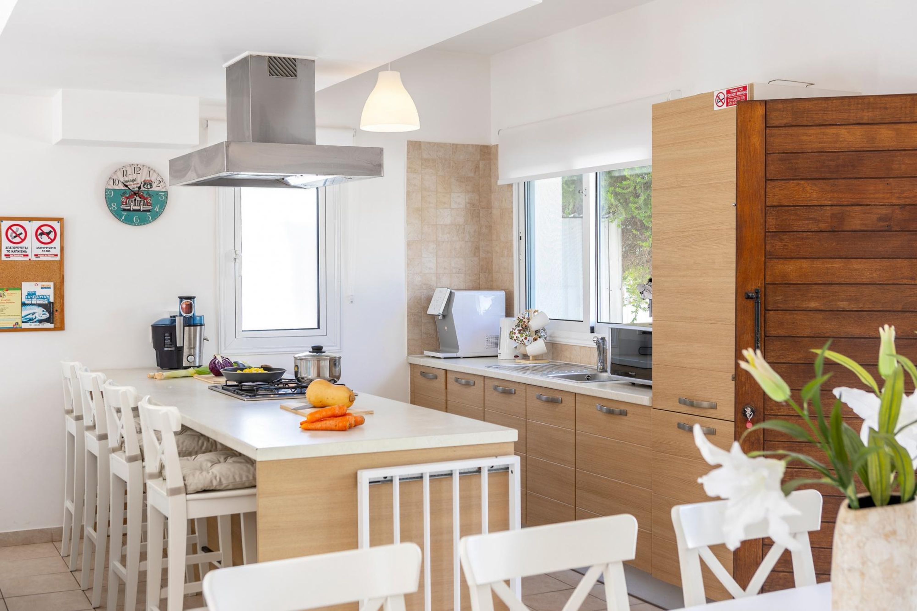 Cozinha moderna com armários brancos, uma ilha central com assentos, coifa de aço inoxidável e uma janela que proporciona luz natural.