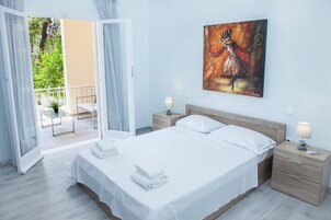 Quarto de hotel com uma cama, duas mesas de cabeceira, um quadro e uma varanda com uma mesa e cadeiras.
