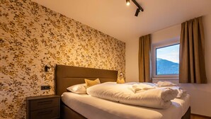 Quarto de hotel com cama grande, mesa de cabeceira, luminária na parede e janela com cortinas.