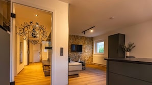 Um interior moderno com piso de madeira, área de jantar com mesa e cadeiras, sofá, TV fixada na parede e janela com vista.