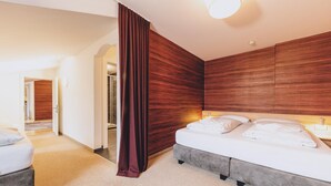 Quarto de hotel moderno com uma cama grande, área de estar separada e um painel de parede em madeira.