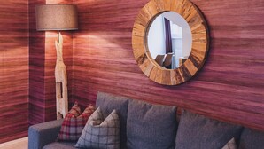 Quarto com parede de madeira, espelho redondo, luminária e sofá cinza com almofadas.
