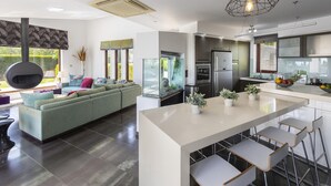 Uma cozinha moderna com ilha central, eletrodomésticos de aço inoxidável e área de estar com sofá e cadeiras.