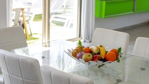 Uma mesa de jantar com uma fruteira, cadeiras brancas e bancada de cozinha verde.