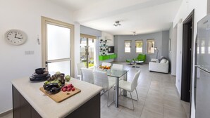 Cozinha moderna com área de refeições, com ilha central, alimentos frescos, geladeira embutida e parede verde decorativa.