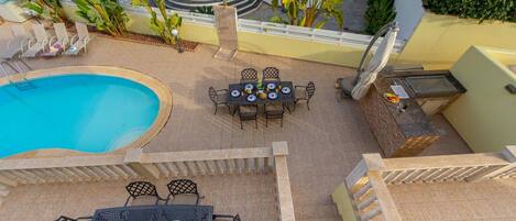 Uma área de piscina no terraço com mesa e cadeiras, uma piscina pequena e vegetação ao redor.