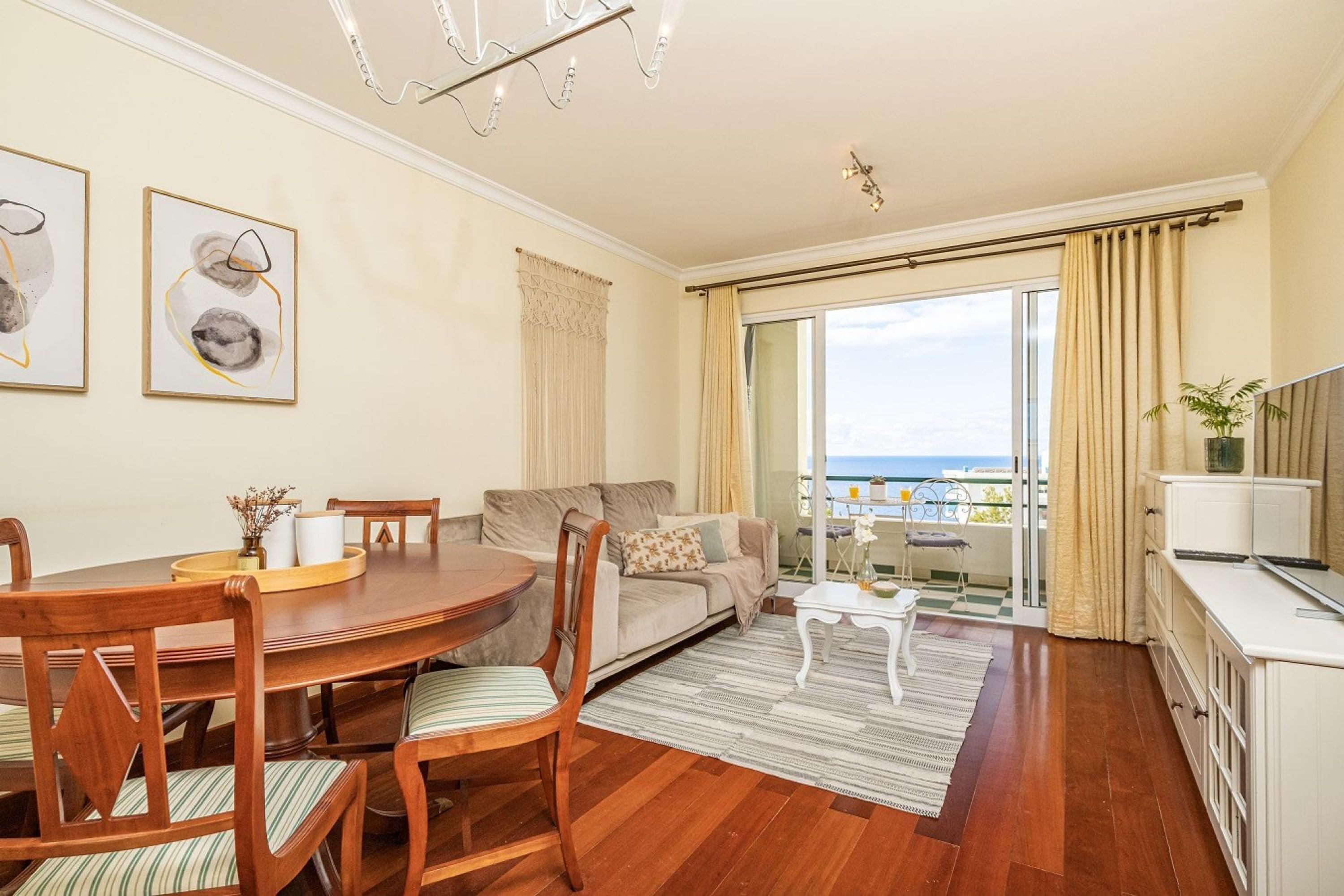 Uma sala de estar moderna com uma mesa de jantar de madeira, sofá e varanda com vista para o mar.