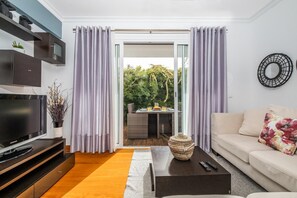 Uma sala de estar moderna com televisão de tela plana, um sofá, uma mesa de centro e um espaço de jantar com mesa e cadeiras.