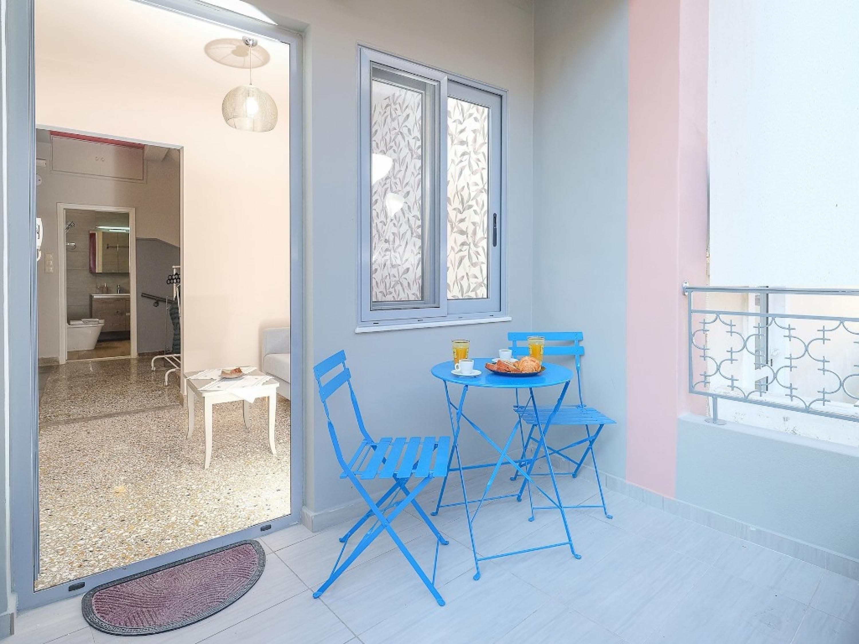 Uma varanda com mesa e cadeiras, uma janela com vidro fosco e vista para um banheiro.