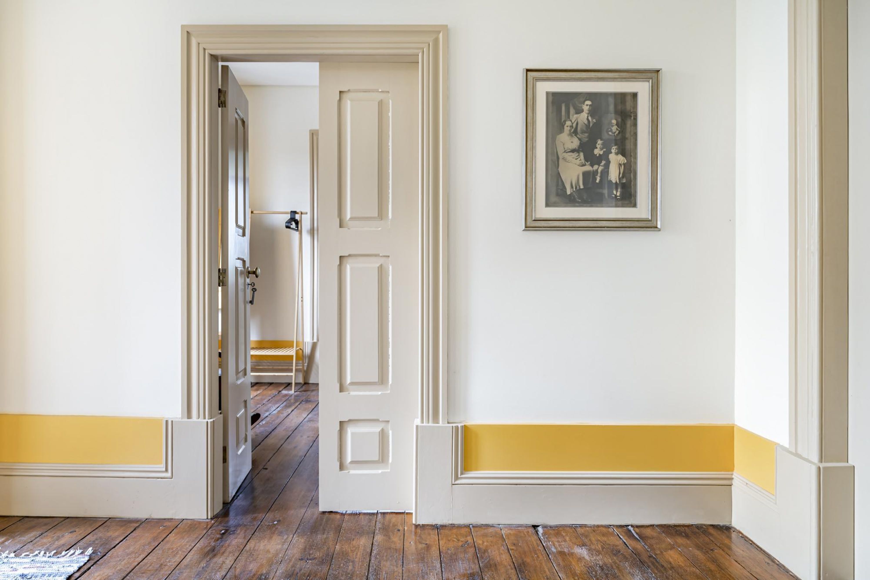 Um corredor com piso de madeira, paredes brancas e um quadro na parede.