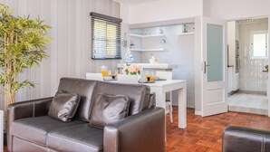 Uma sala de estar moderna com um sofá de couro, uma mesa de jantar com itens de café da manhã e uma cozinha visível por uma porta aberta.